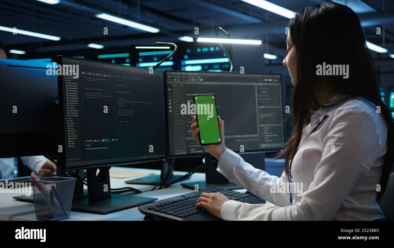 Worker overseeing data center using green screen mobile phone, ensuring system can handle ...