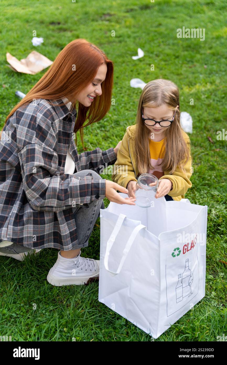 Little girl and teacher working together in park collecting glass waste ...