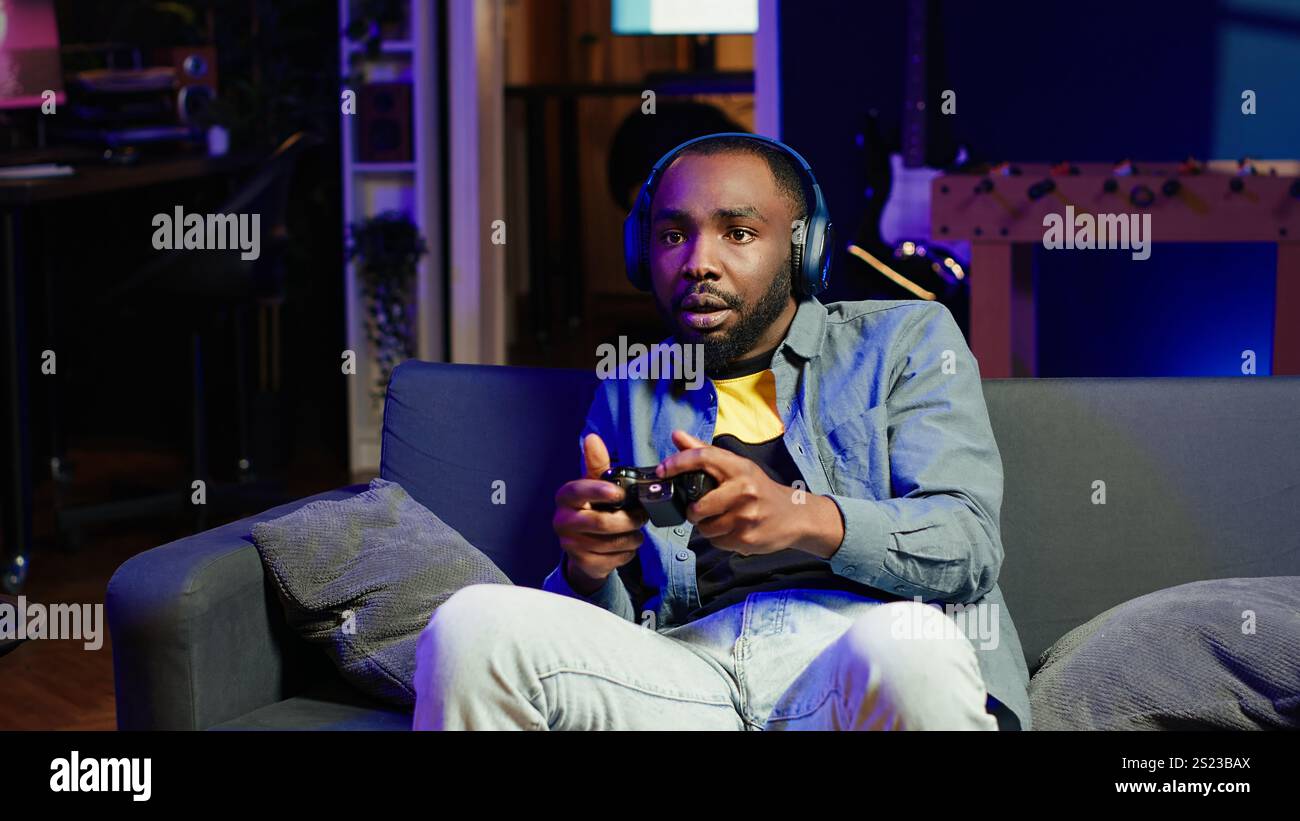 Enthusiastic gamer on couch using controller and headphones to play ...