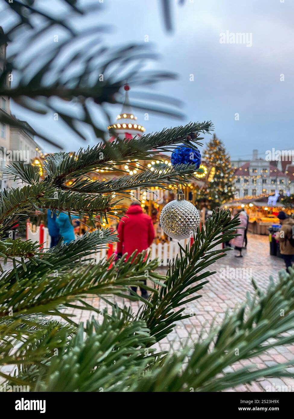 Christmas market and carousel seen through fir branches and ornaments ...