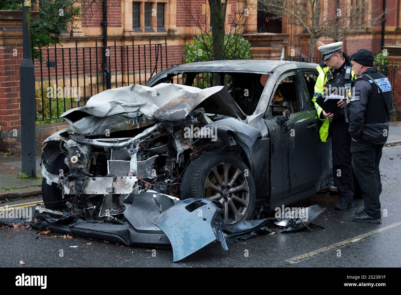 Met police officers inspect the burned-out wreck of a car which remains ...