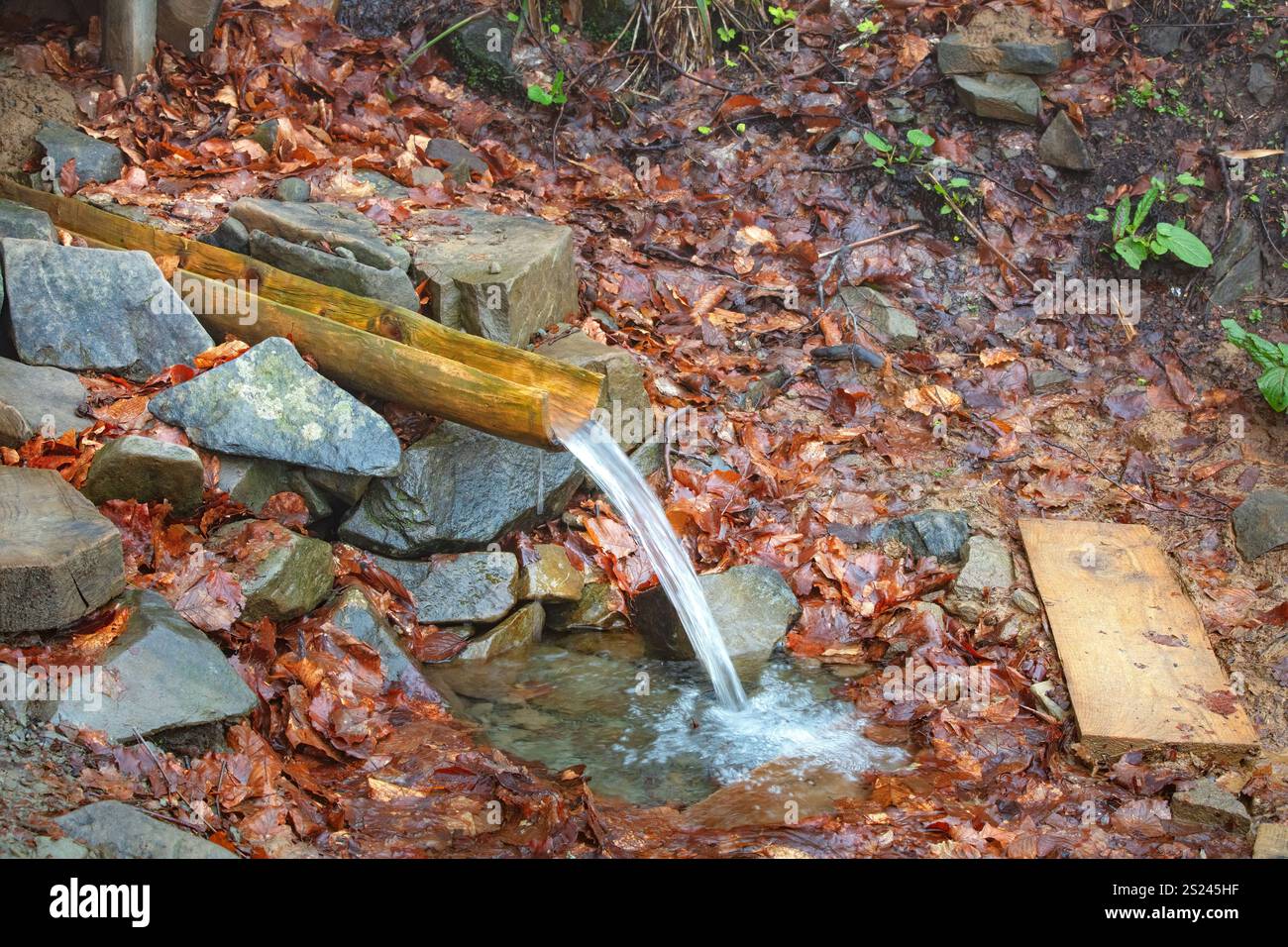 Clear water cascades from a wooden trough, creating a soothing sound as ...