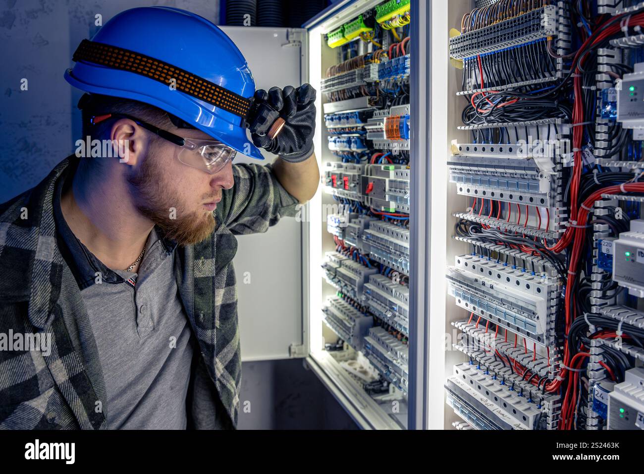 A male electrician works in a switchboard in overalls against the ...
