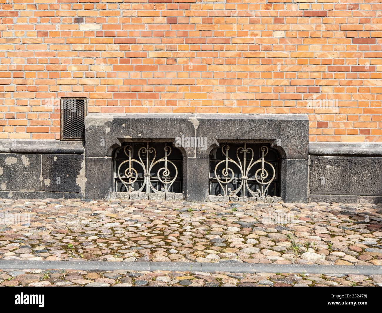 Brick wall with vintage metal window grating over a cobblestone path ...