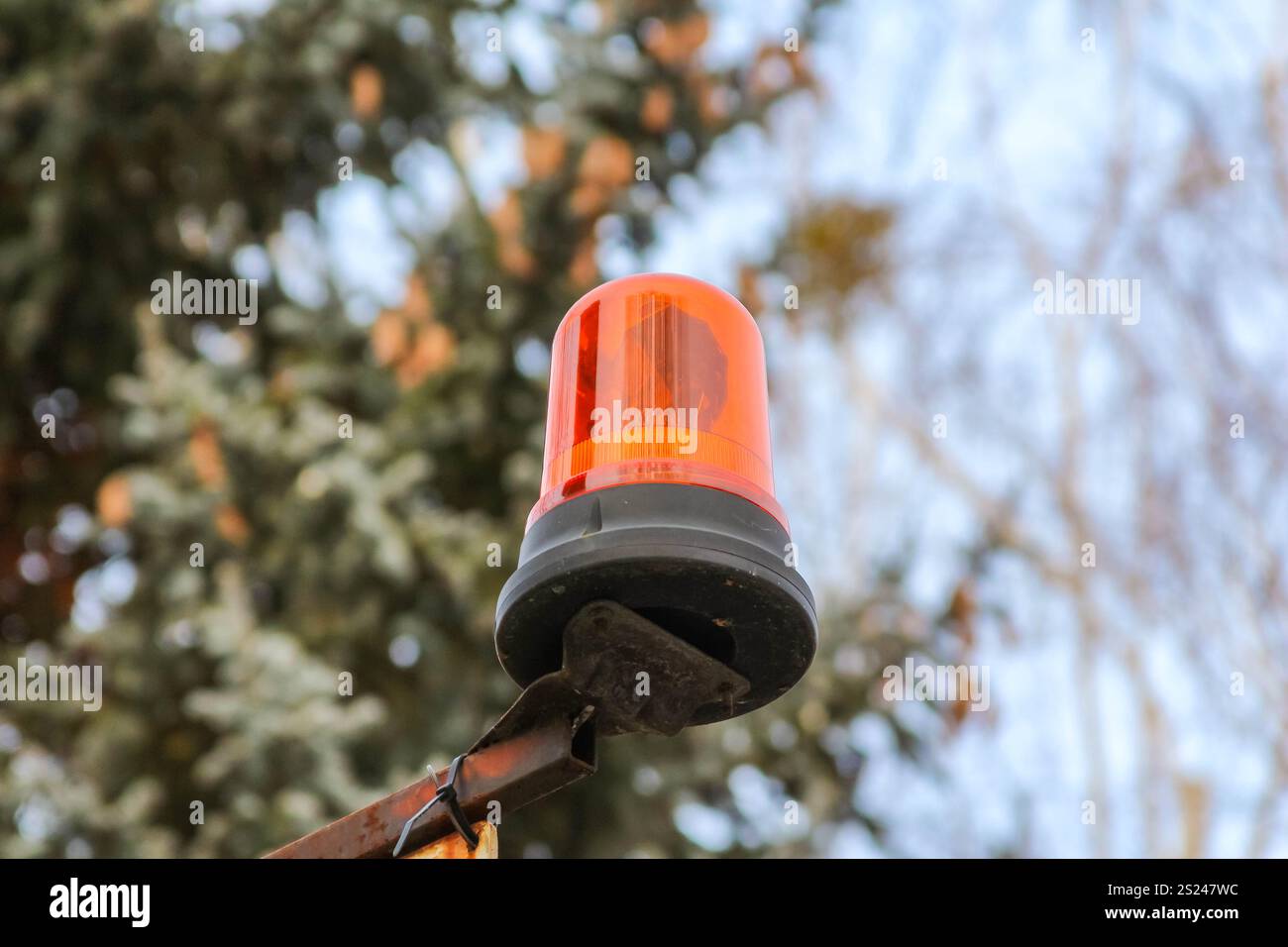 Bright orange warning light sits on a pole against a backdrop of snowy ...