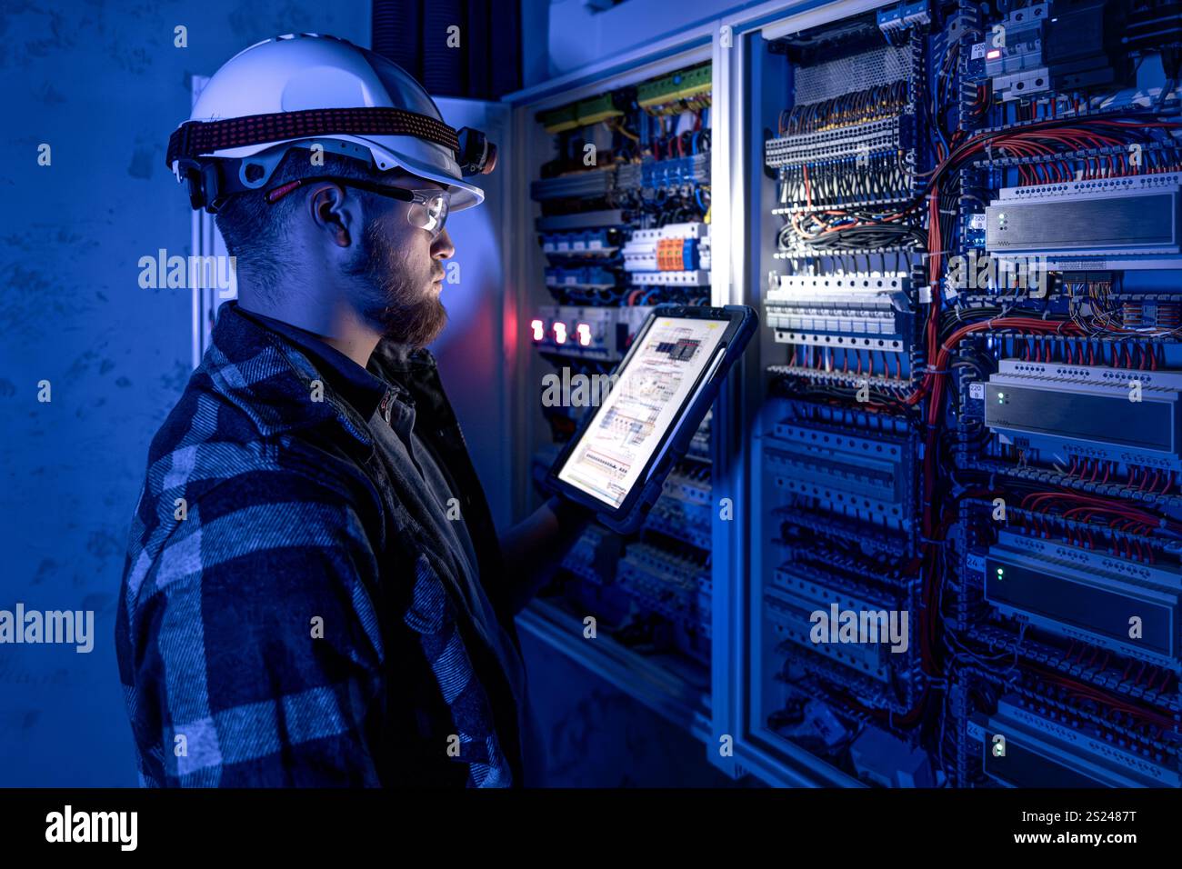 Electrician in overalls, focused on work in switchboard with fuses ...