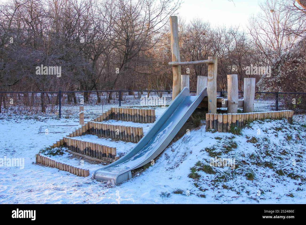 A wooden slide sits on a snowy playground surrounded by trees, inviting ...