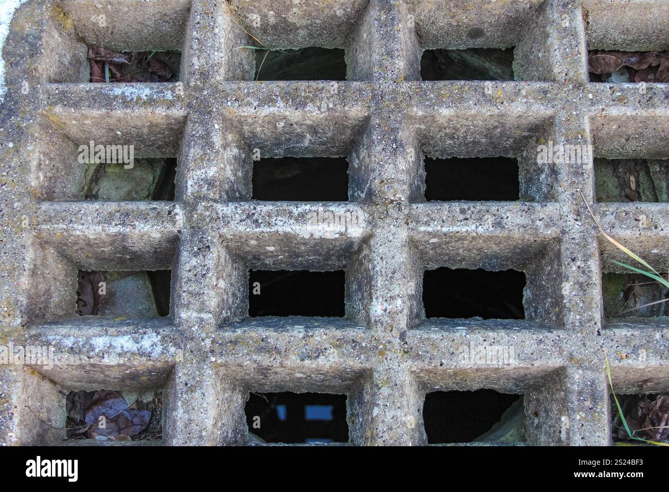 A close-up of a concrete drainage grate reveals a detailed grid pattern ...