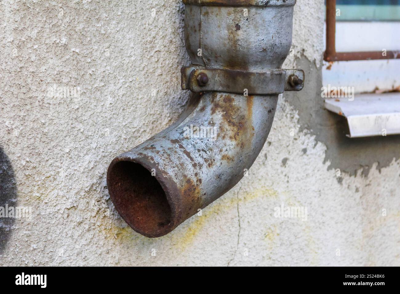A worn metal pipe curves from a weathered wall, showing signs of rust ...