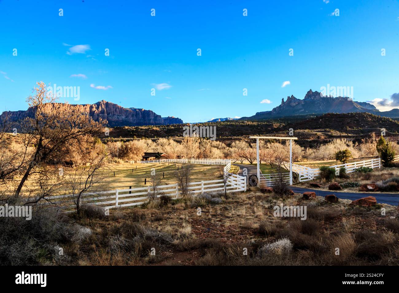 A large, open field with a white fence and a gate. The sky is blue and ...