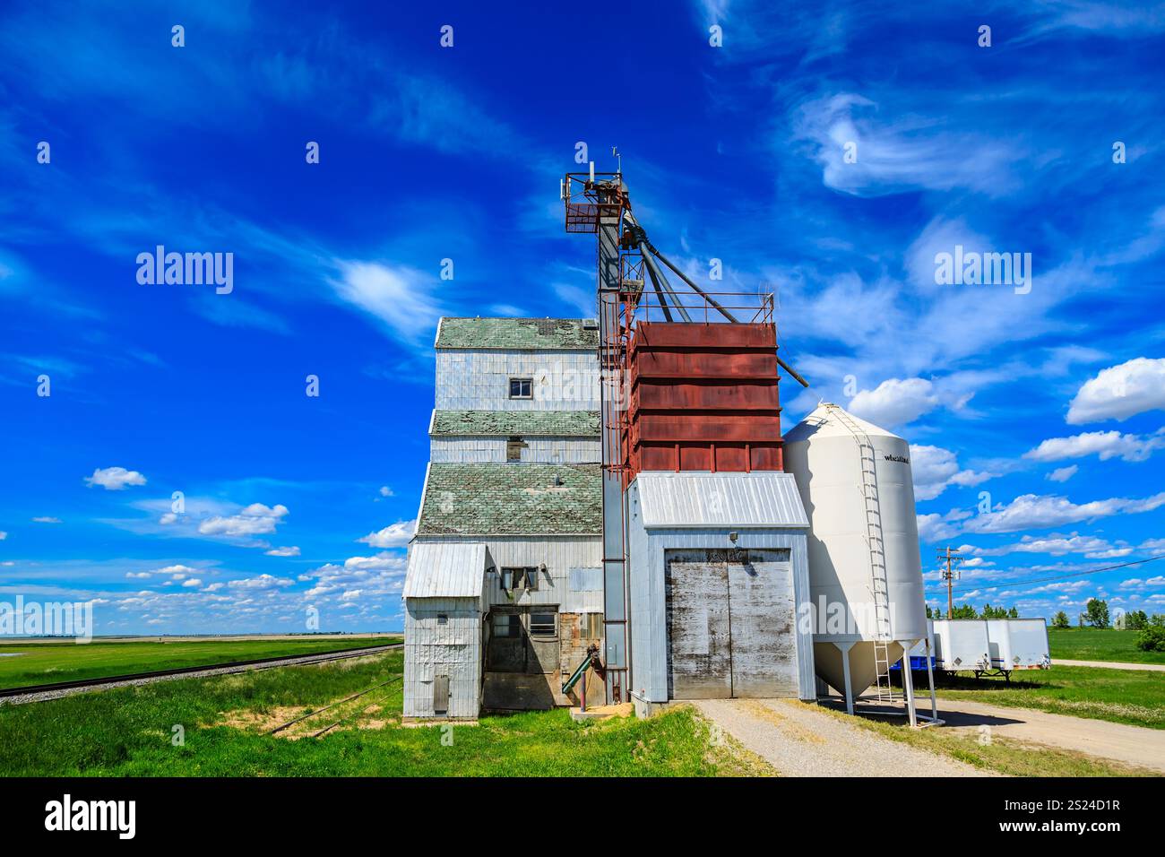 A grain silo is surrounded by a field and the sky is blue. The silo is ...