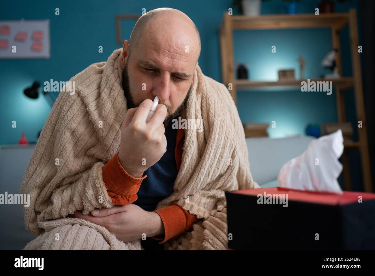 Sick middle aged man wrapped in blanket uses nasal spray feels like he ...
