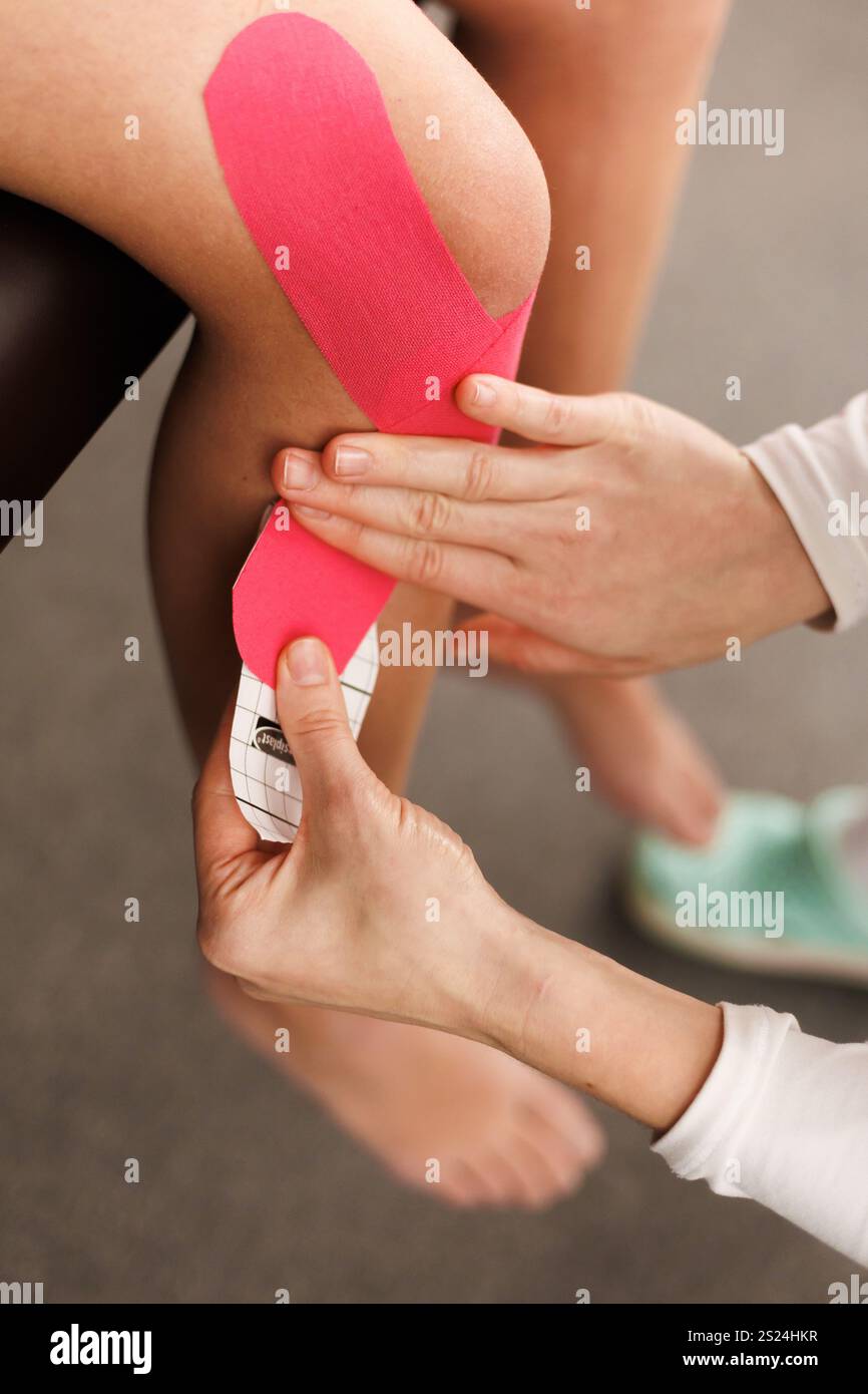 doctor taping female knee applying kinesiology tape to patient knee. Therapist treating young ...