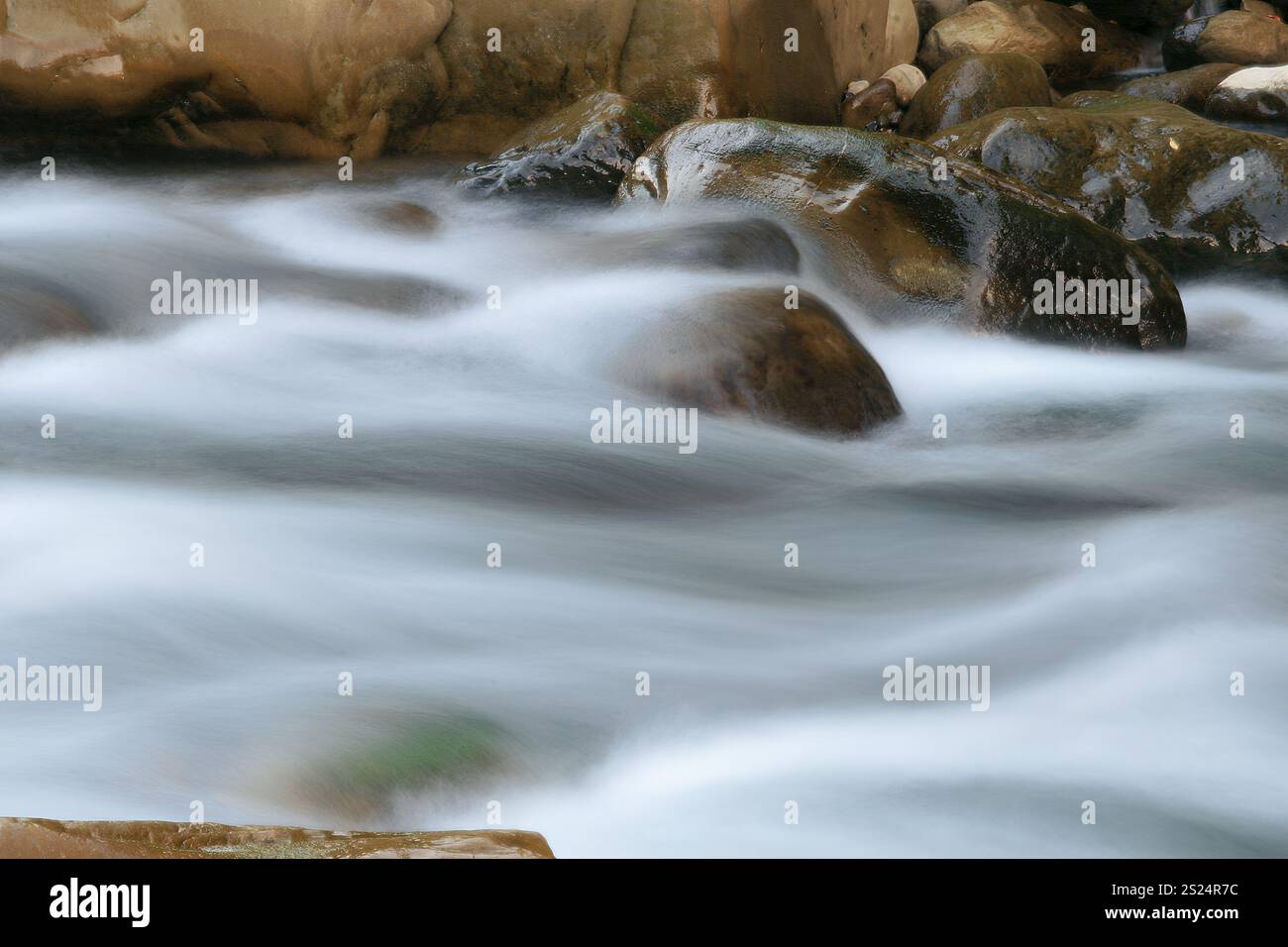 A fast-flowing river rushes over smooth and rough rocks, creating a ...