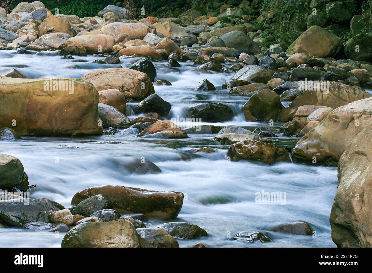 A fast-flowing river rushes over smooth and rough rocks, creating a ...