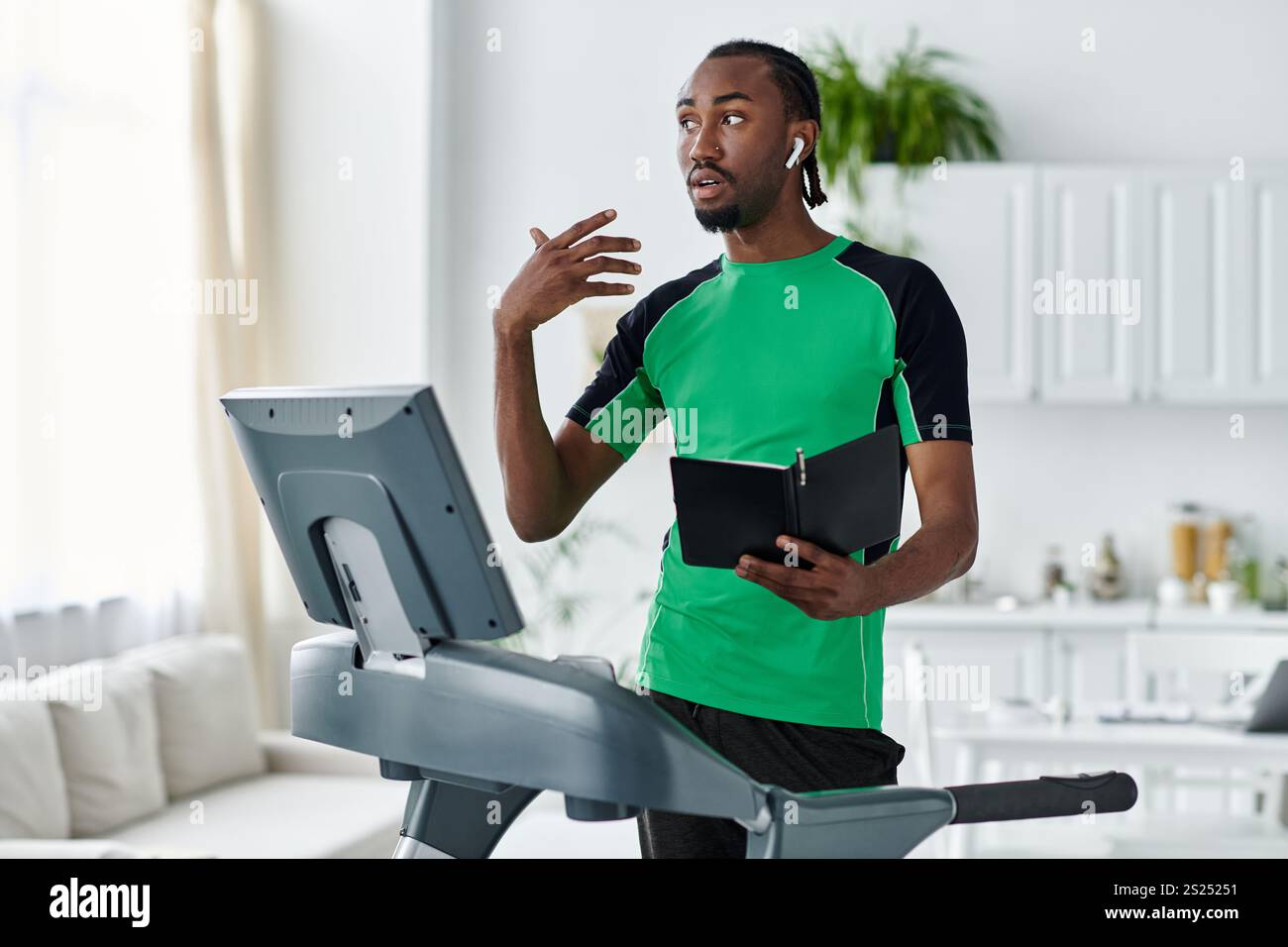 A young African American man multitasks by exercising on a treadmill ...