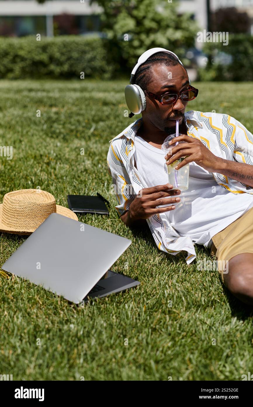Casual workday in the park for a young man, relishing a drink and music ...