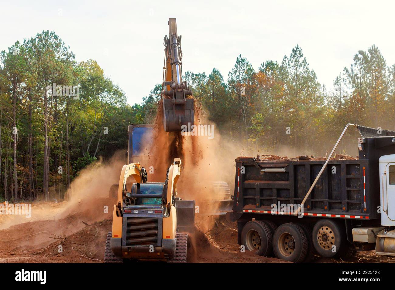 Heavy machinery works together to load dirt into dump truck under ...