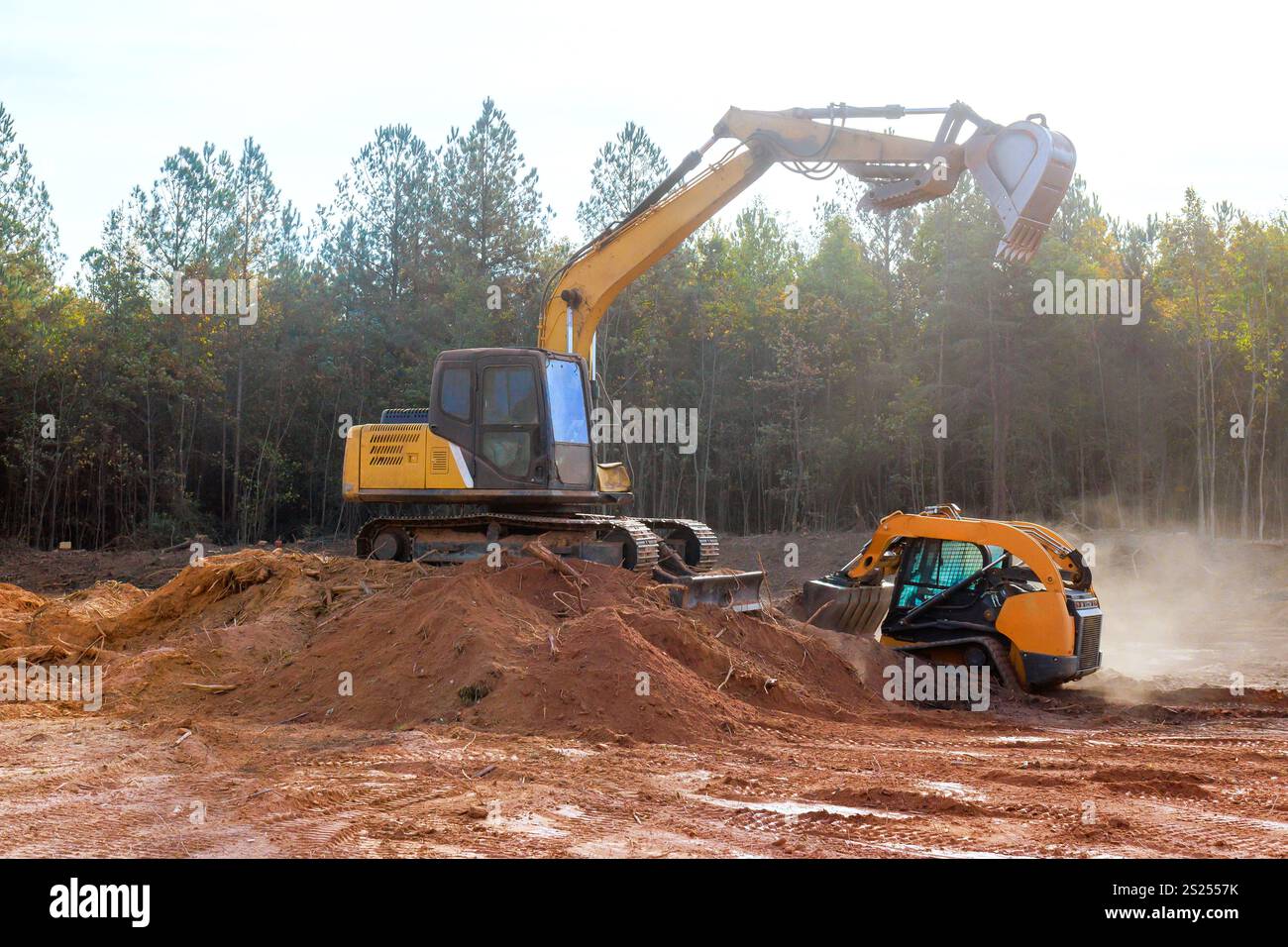 Heavy machinery with bulldozer, excavator performs land clearing on construction site, at dust ...