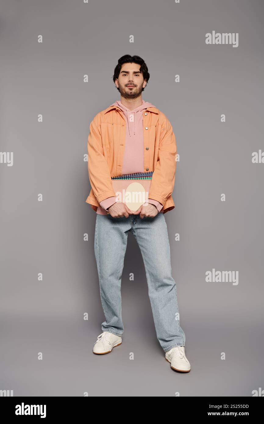 Stylish young man stands confidently, holding a notebook in a studio ...