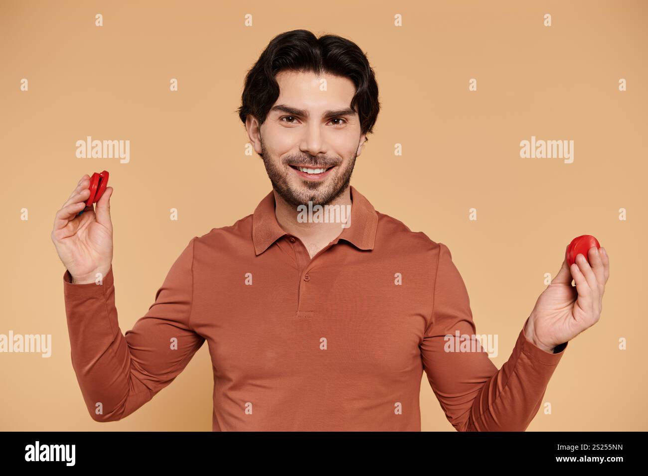 A cheerful young man holds red objects in both hands, radiating joy and ...