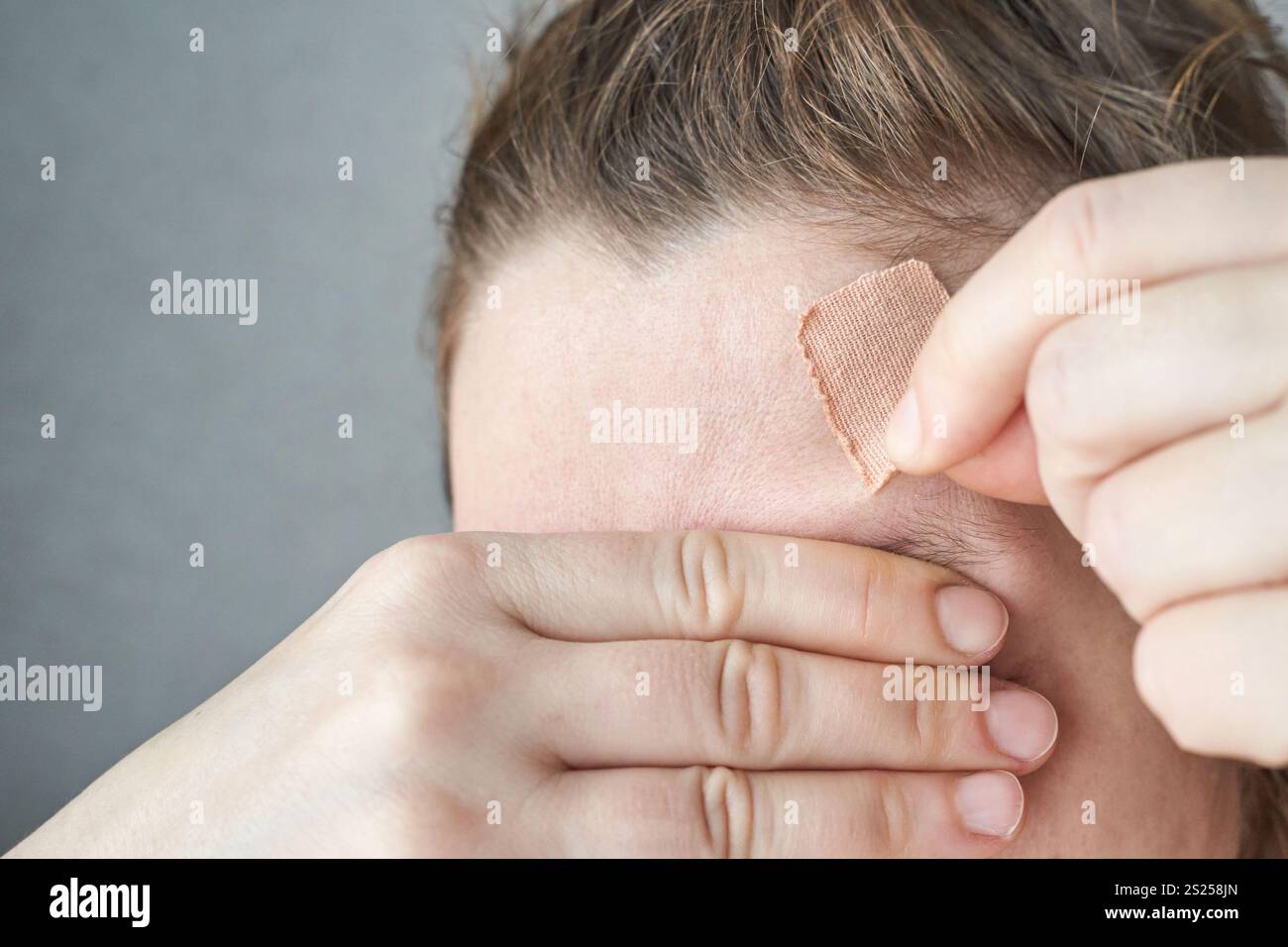 Female adult with bandage on forehead covering eyes with hand ...