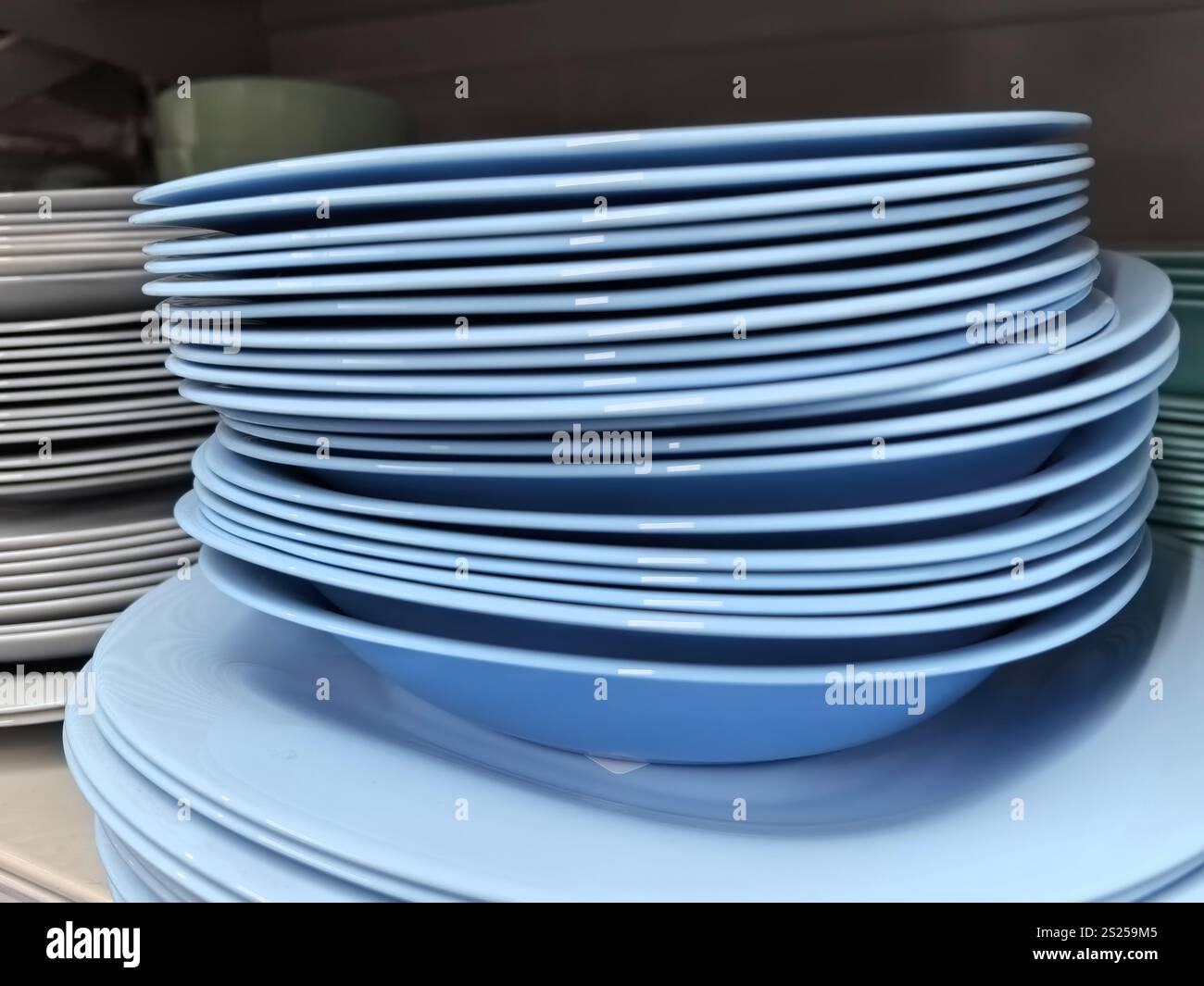 A collection of neatly stacked blue plates rests on a shelf, reflecting ...