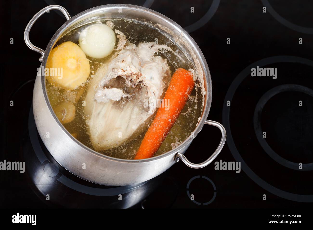 boiling of chicken soup with seasoning vegetables in steel pan on glass ...