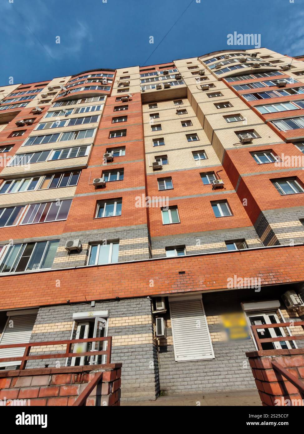 A tall red and beige brick residential building with multiple balconies ...
