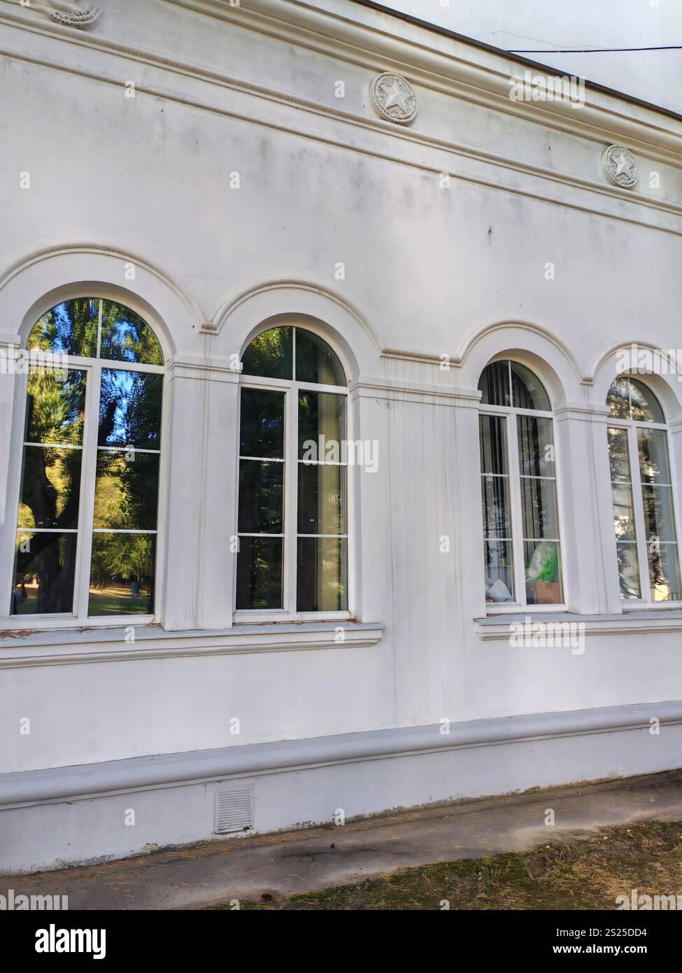 A white structure with tall arched windows partially obscured by trees ...