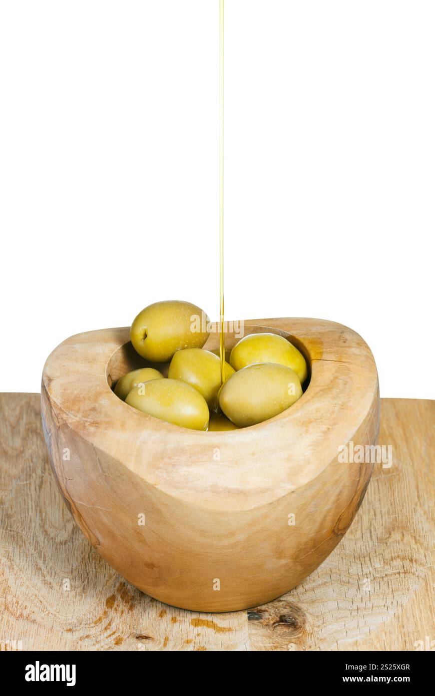 olive oil in thin trickle flows on olives in wooden bowl close up ...