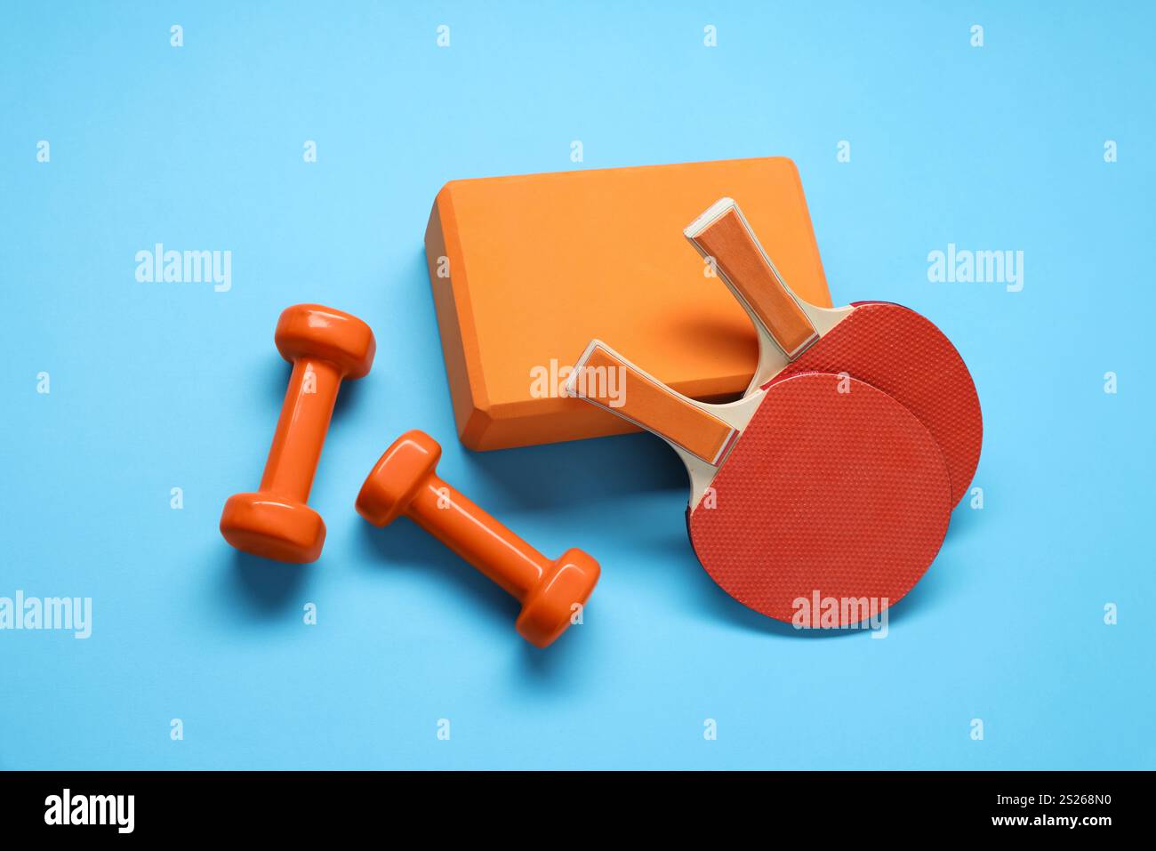 Dumbbells, yoga block and ping pong rackets on light blue background ...