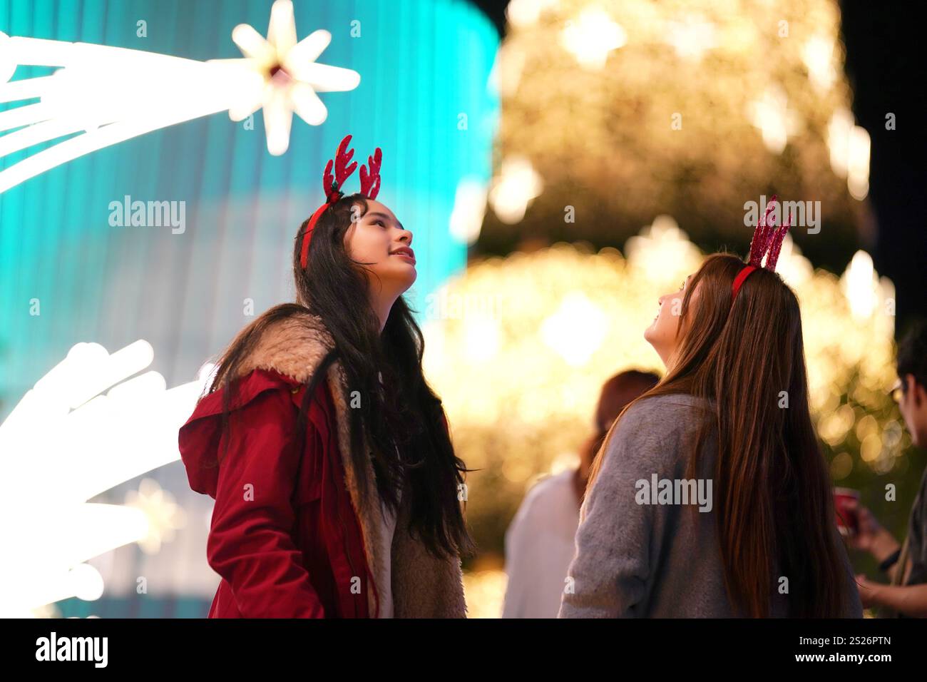 Two friends stand close together, delighted by the dazzling holiday ...