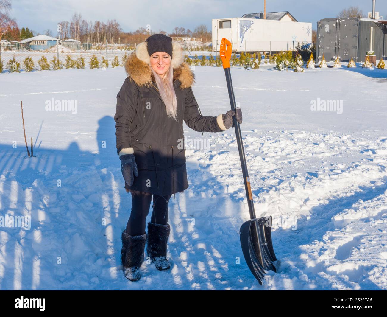 Woman shoveling snow, bundled in winter gear, smiling while clearing ...