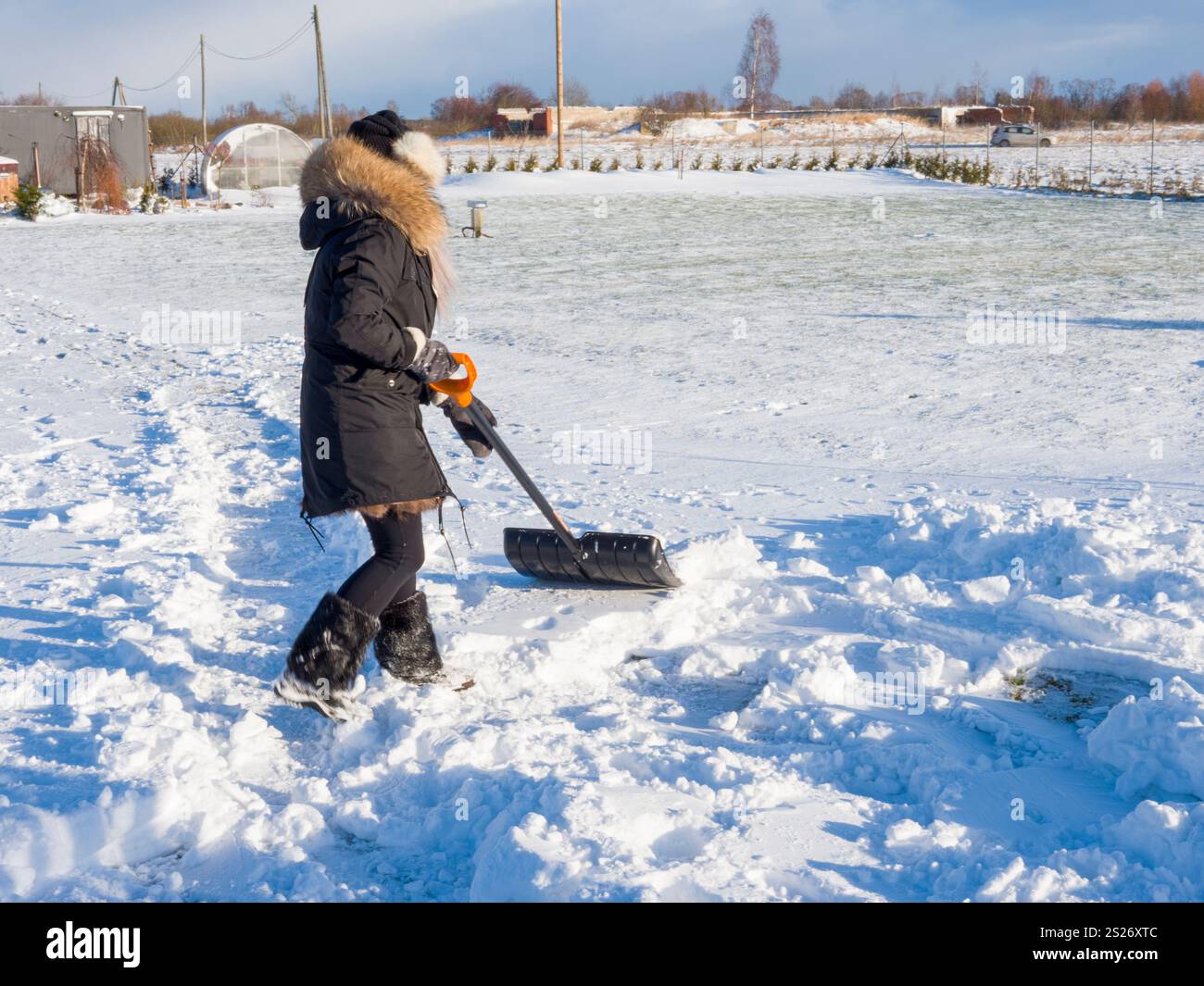 Woman wearing heavy winter gear shoveling snow in bright sunlight ...