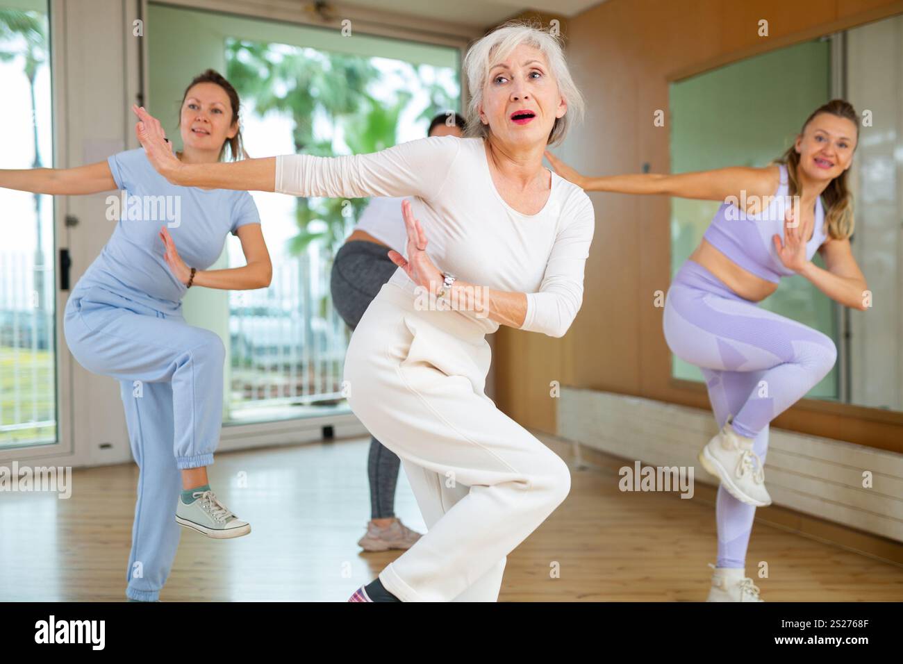 Mature female coach dancing and practicing new movements with group of ...
