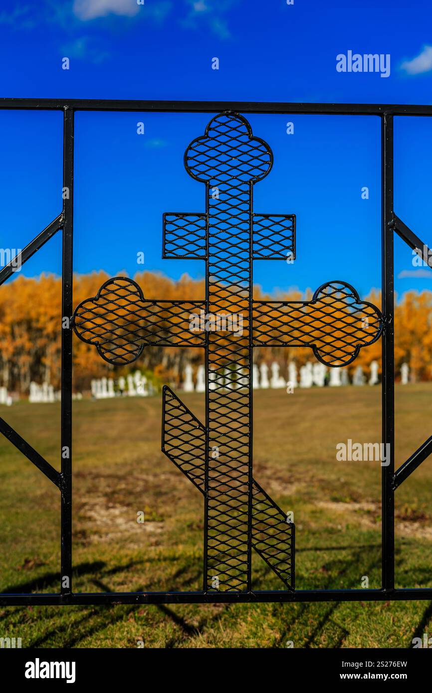 A metal cross with a mesh design is on a fence. The fence is surrounded ...