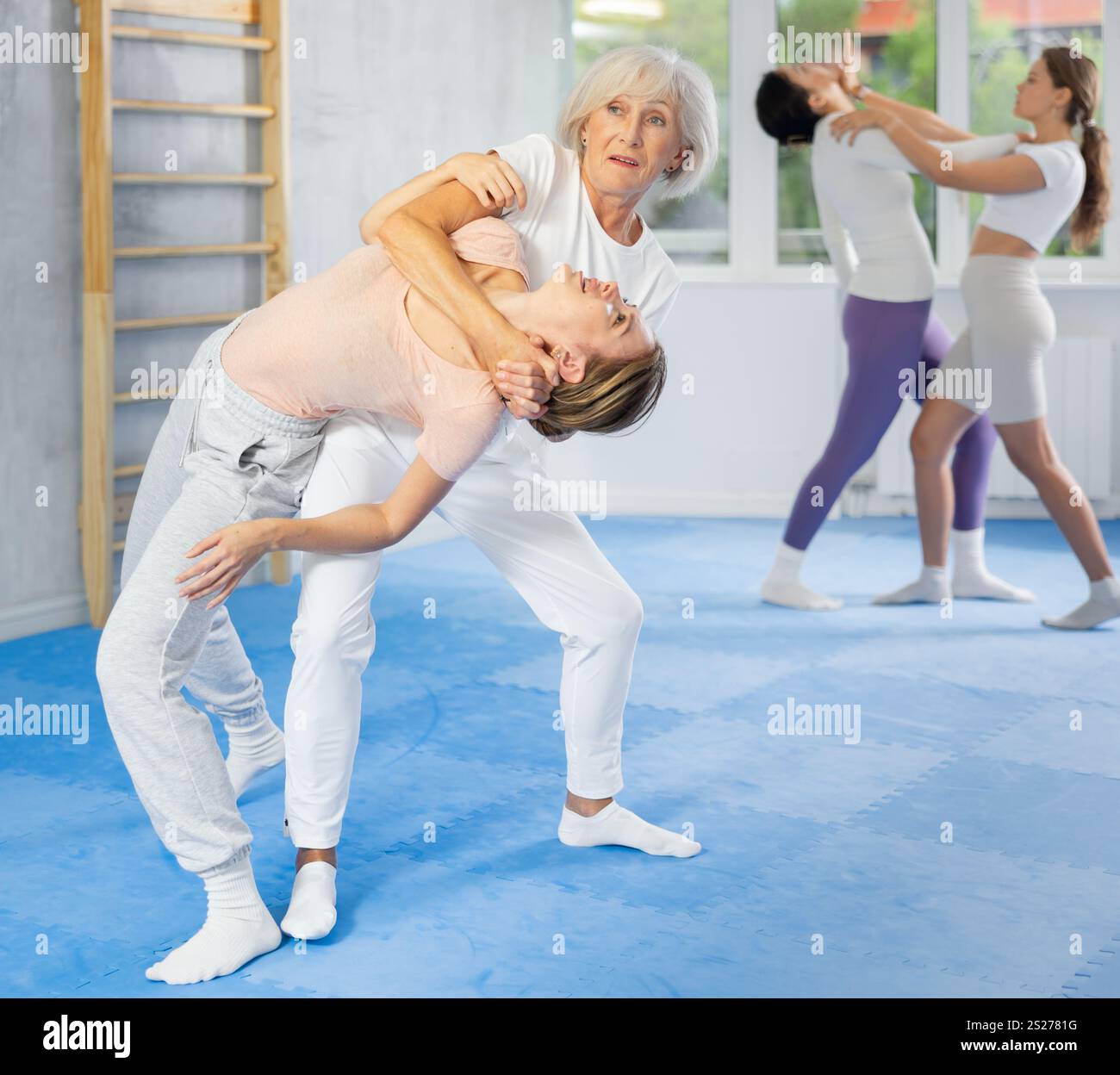 Senior woman applying inverted headlock during mock bout in self ...