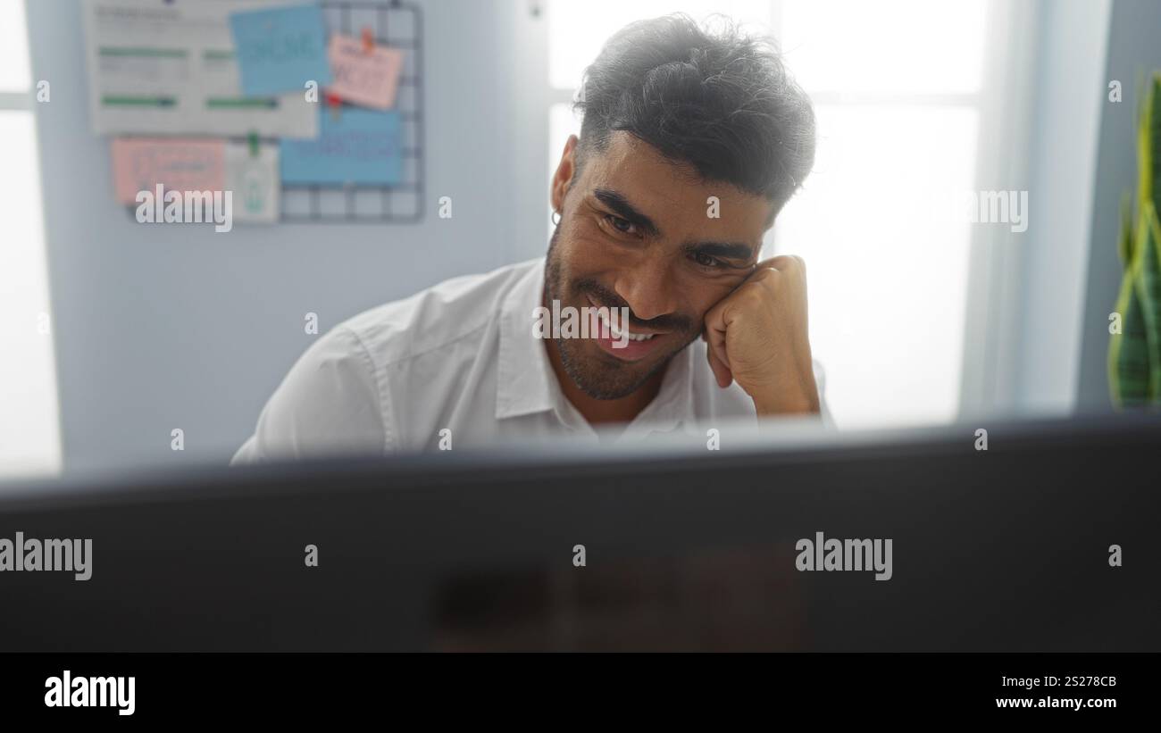 Young man smiling while working at a computer in an office interior ...