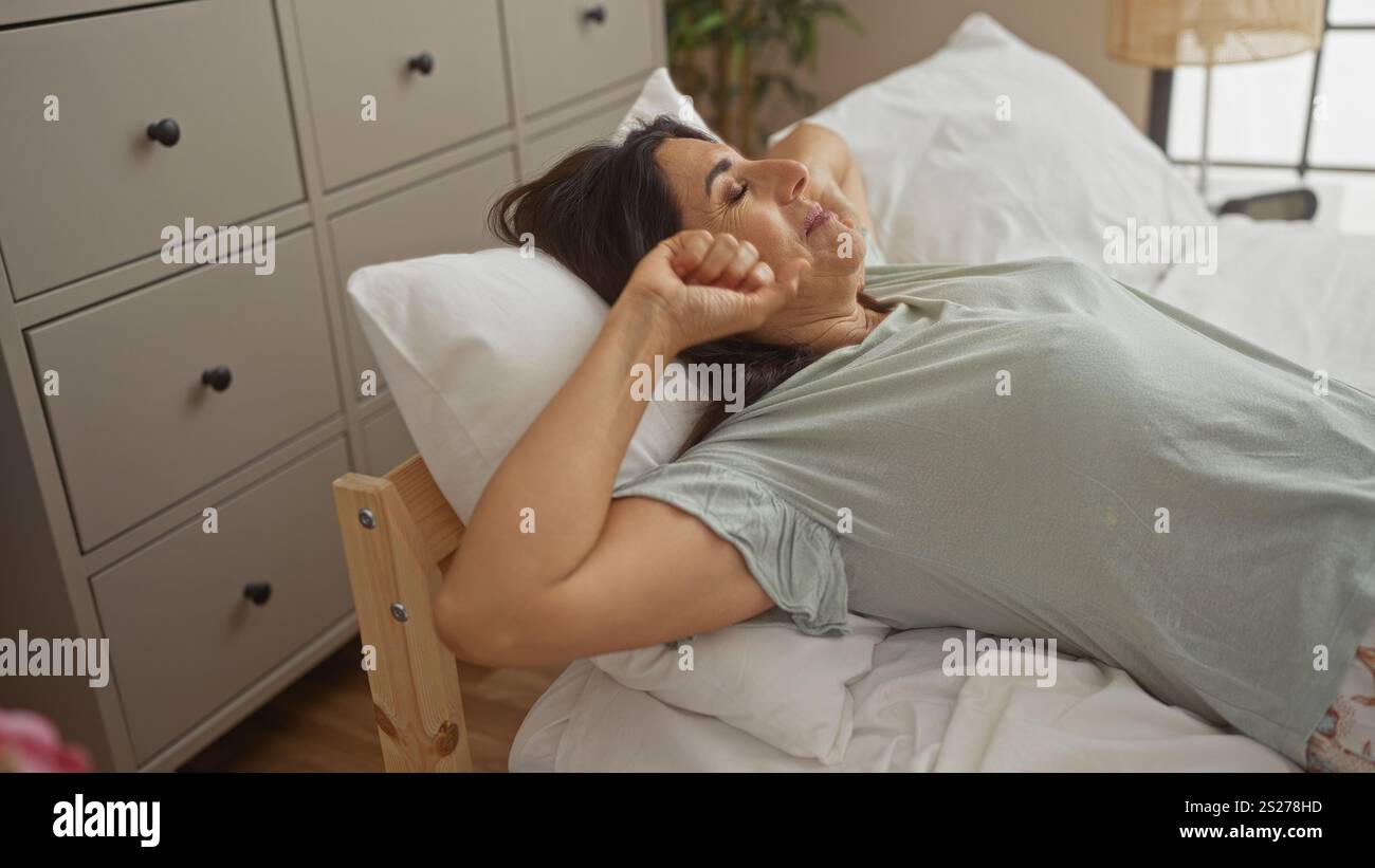 Woman waking up and stretching in bed inside a cozy bedroom, wearing a ...