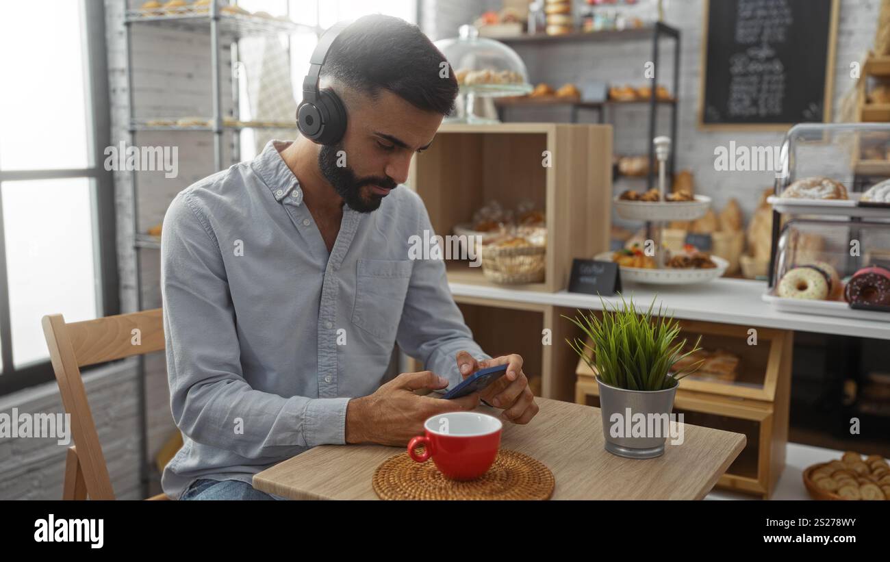 Young hispanic man with a beard and headphones at a bakery using his ...