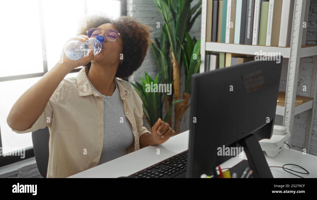 Woman drinking water in office room with curly hair seated at desk ...