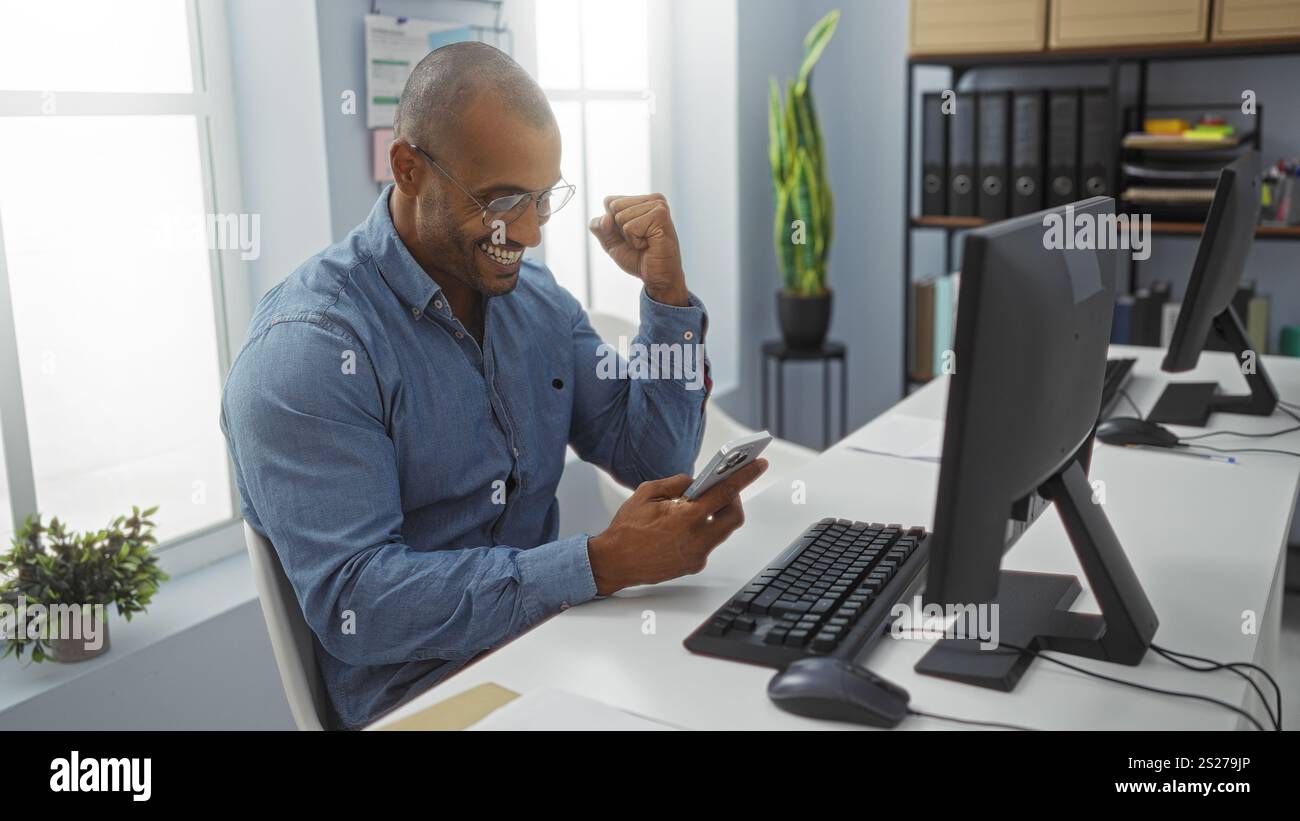 Young man excitedly checks smartphone at desk in modern office ...
