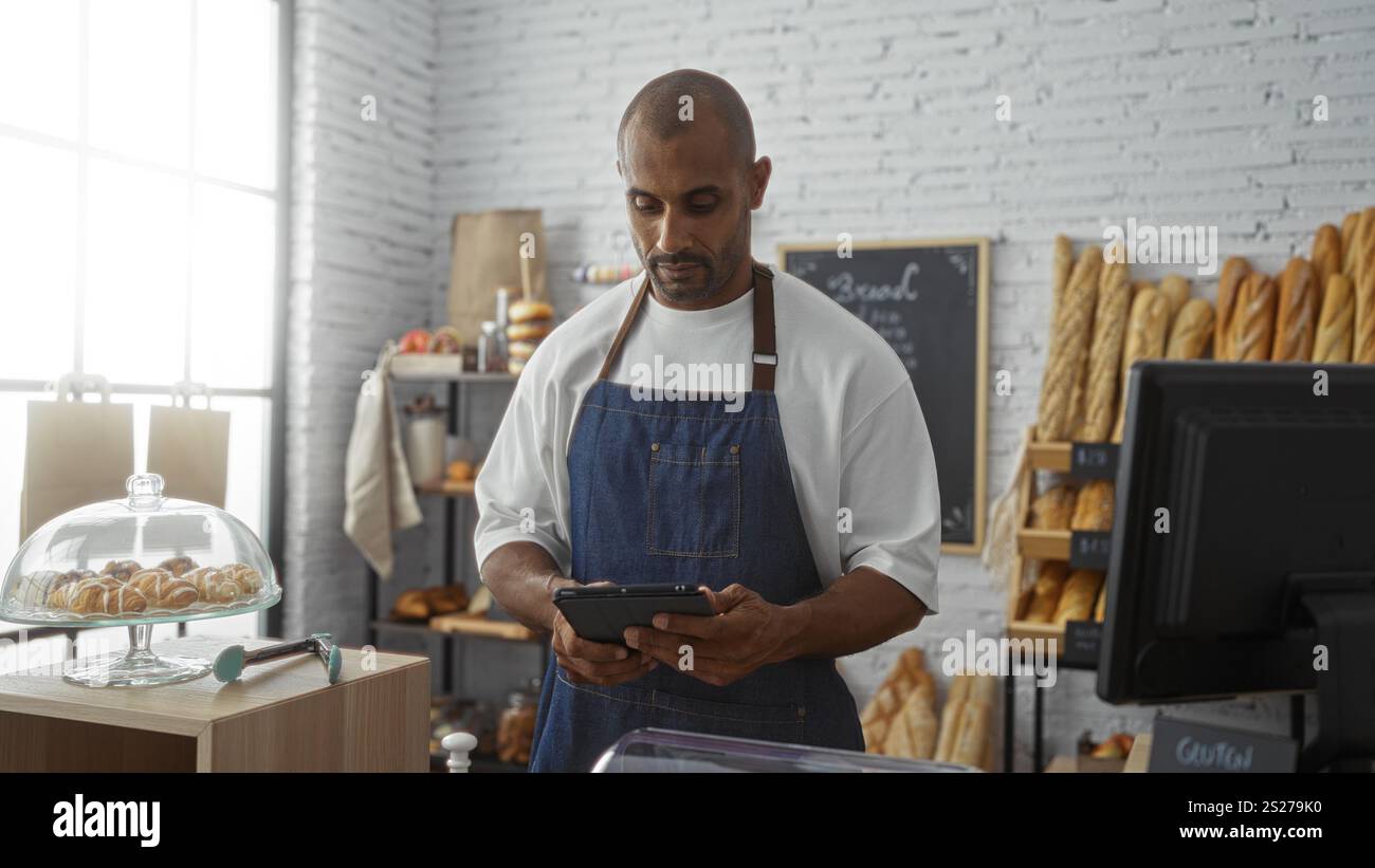 Handsome young man using tablet in a bakery surrounded by shelves of ...