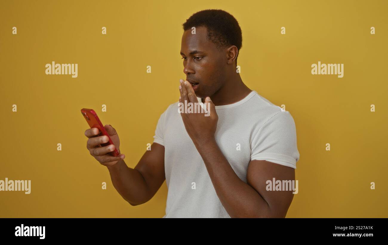 Young man holding smartphone looking surprised against yellow ...