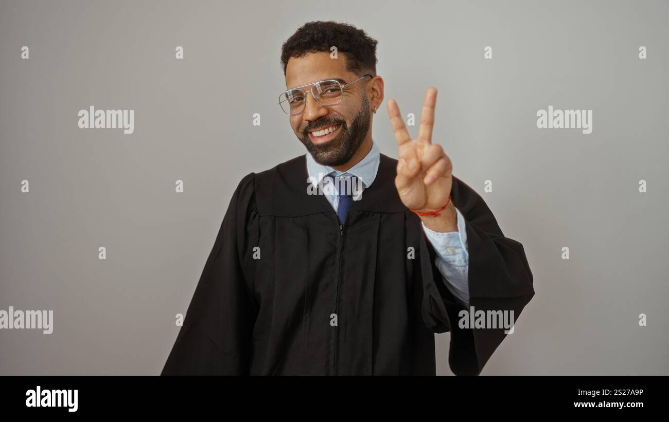 Hispanic male graduate in cap and gown smiling and making a peace sign ...