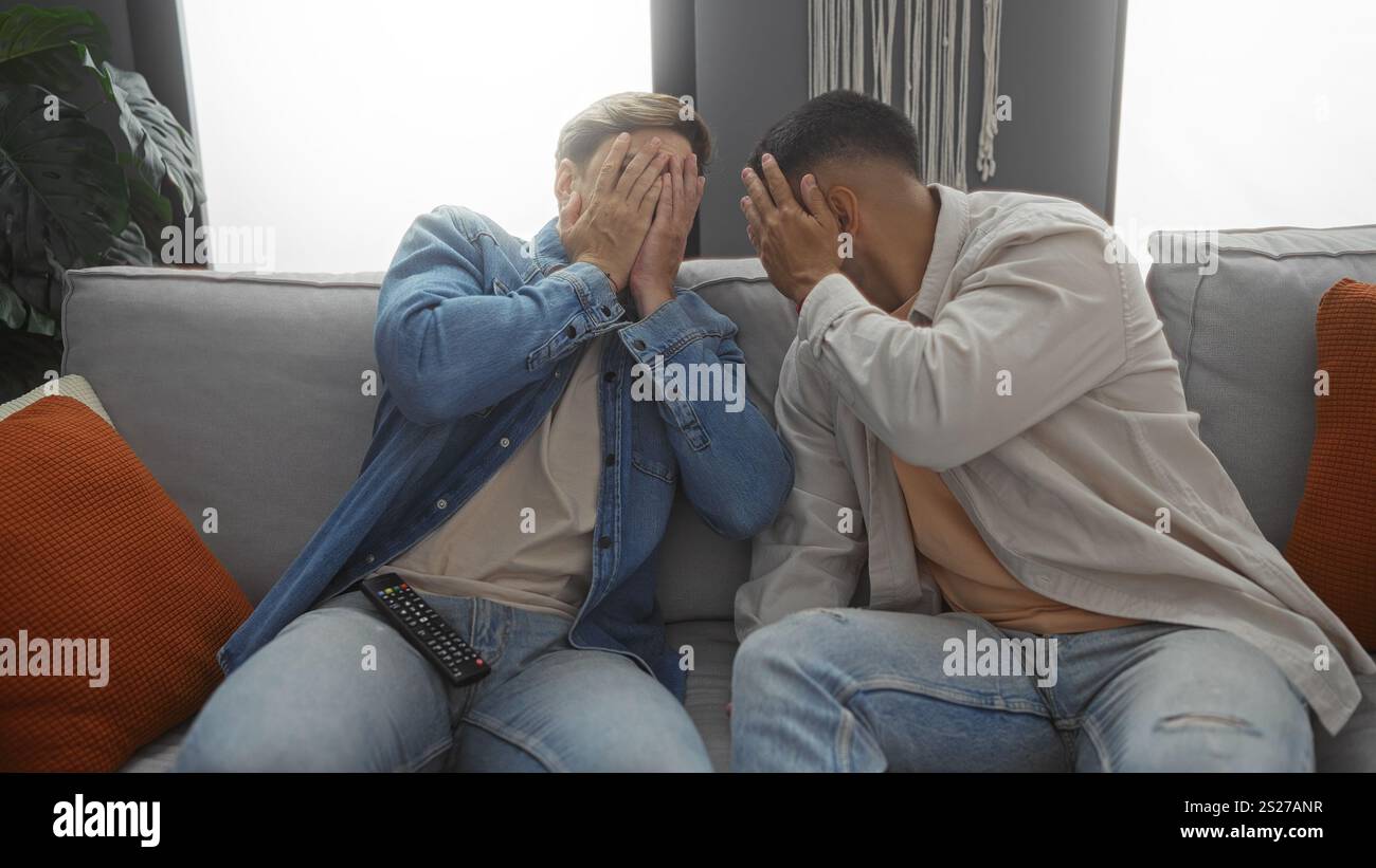 Two men sit on a couch covering their faces in fear while watching a ...