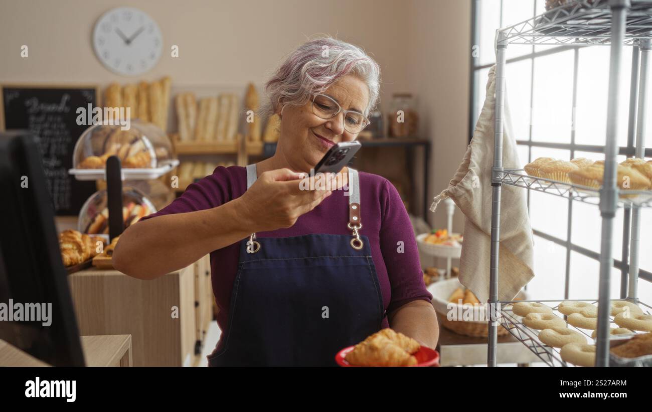 Grey-haired woman taking a photo of a pastry in a bakery with breads ...