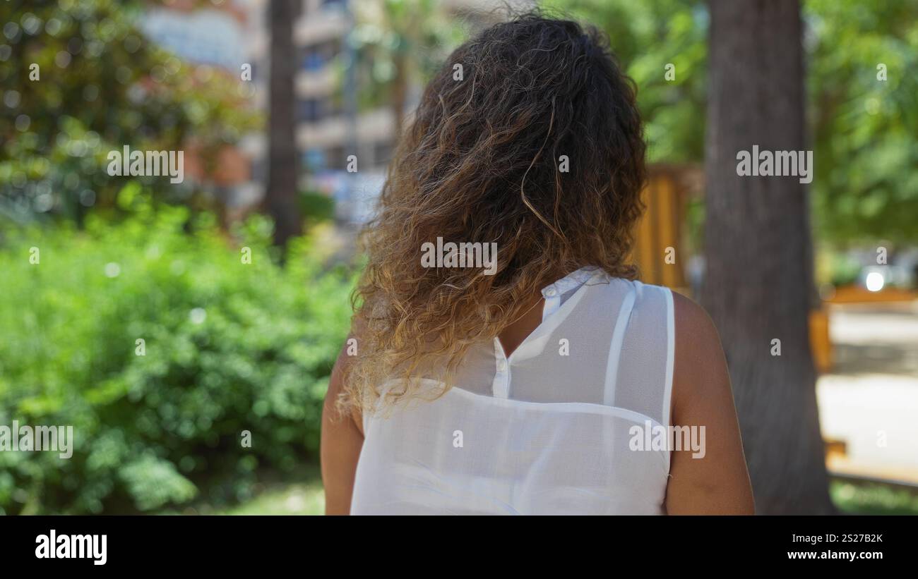 Woman seen from behind standing outdoors in an urban park, with a ...