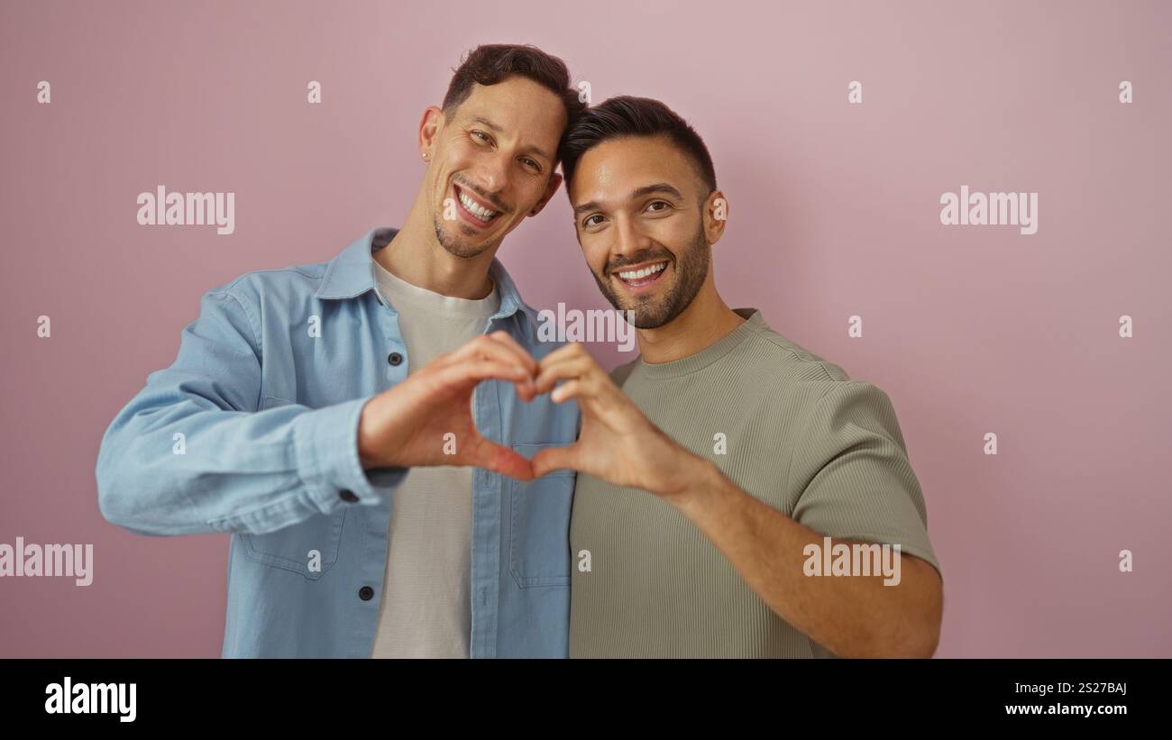 Men gay couple making heart shape with hands smiling together on pink ...